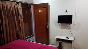 Quarto com cama, televisão na parede, porta de madeira e cortina.