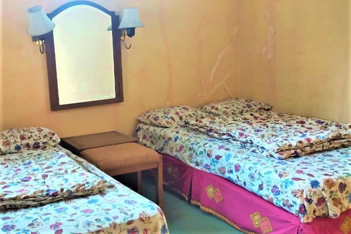 Quarto com duas camas, um banquinho, um espelho e luminárias na parede.