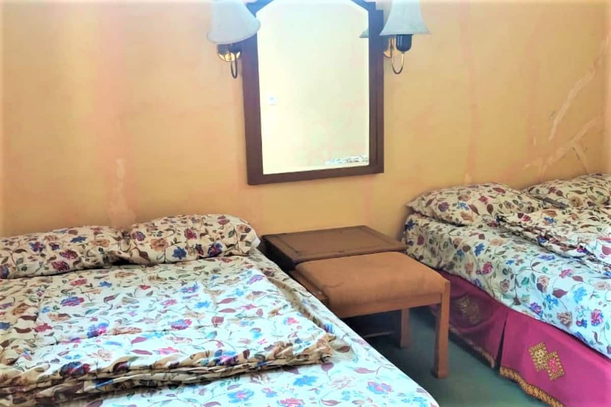 Quarto de hotel com duas camas, um pequeno banco de madeira e um espelho fixado na parede, com duas luminárias de parede.