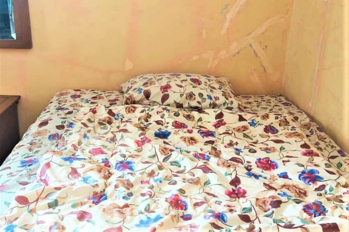 Quarto pequeno com cama de solteiro, colcha e almofadas estampadas com motivos florais.