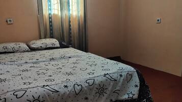 Quarto com cama estampada com padrão de estrela e lua, cortinas e parede revestida em azulejos.