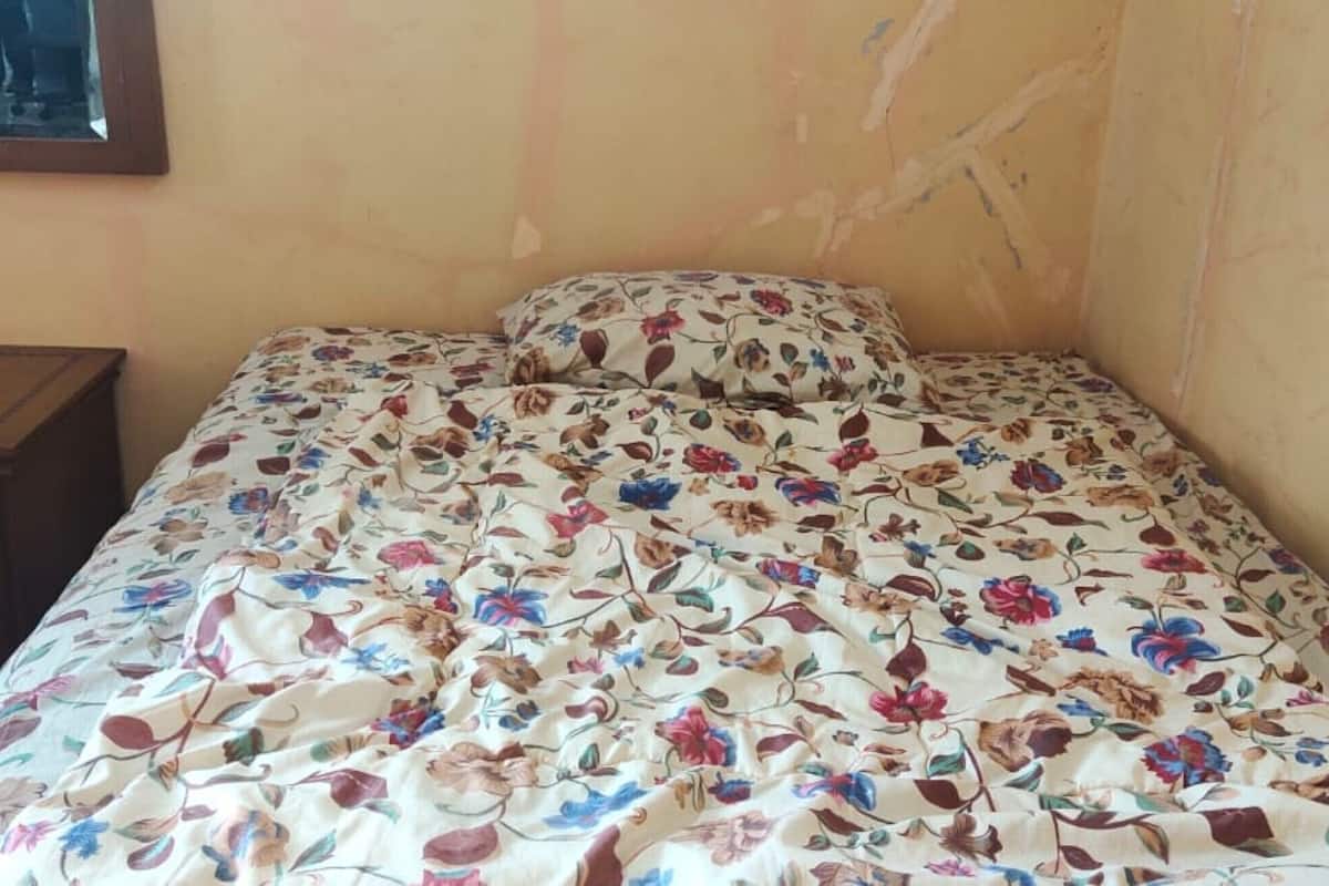 Um quarto pequeno e simples com uma cama, uma mesinha de cabeceira de madeira e um banco.