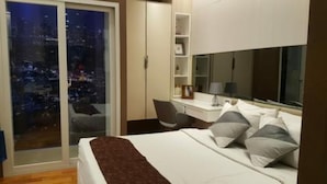 Quarto de hotel moderno com uma cama grande, uma escrivaninha e vista para a cidade pela janela.