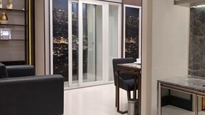 Uma sala de estar moderna com um sofá, uma mesa de jantar com cadeiras e vista para a cidade através de grandes janelas.