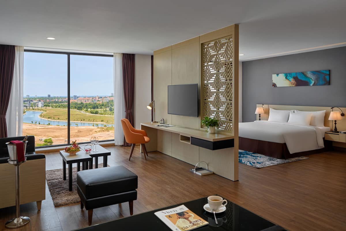Quarto de hotel moderno com uma janela grande, uma escrivaninha, uma cama e uma televisão.