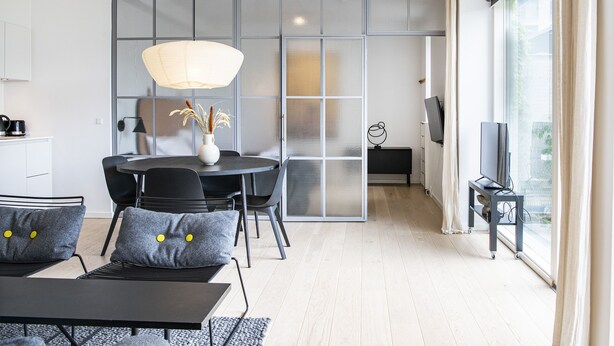 Uma sala de estar moderna com área de jantar, uma janela grande com cortinas e uma televisão sobre um suporte.