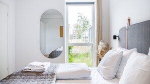 Quarto com cama, janela, espelho e vista para o verde lá fora.