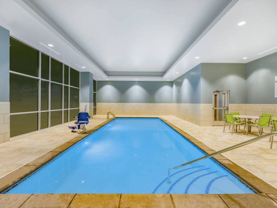 Piscina interna com água cristalina, rodeada por paredes revestidas de azulejos bege e teto com iluminação embutida.
