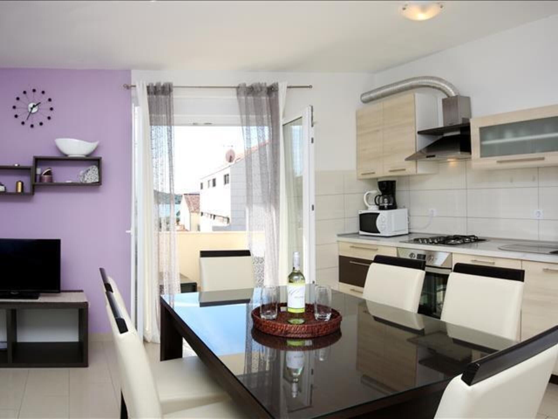 Cozinha moderna com área de jantar, TV e vista através de uma porta de vidro.