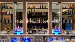 Uma área de bar com várias prateleiras de garrafas de bebidas e copos, um balcão de mármore e um banquinho.