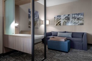 Quarto de hotel moderno com cama, sofá, mesa pequena e arte abstrata na parede.