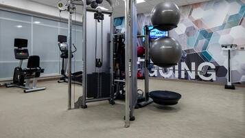 Uma academia com equipamentos de ginástica, uma parede com padrões geométricos e uma tela grande.