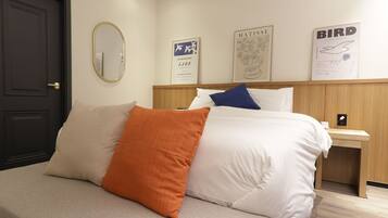 Cama bem arrumada com roupa de cama branca e azul, um travesseiro laranja e uma mesa de cabeceira de madeira com abajur.