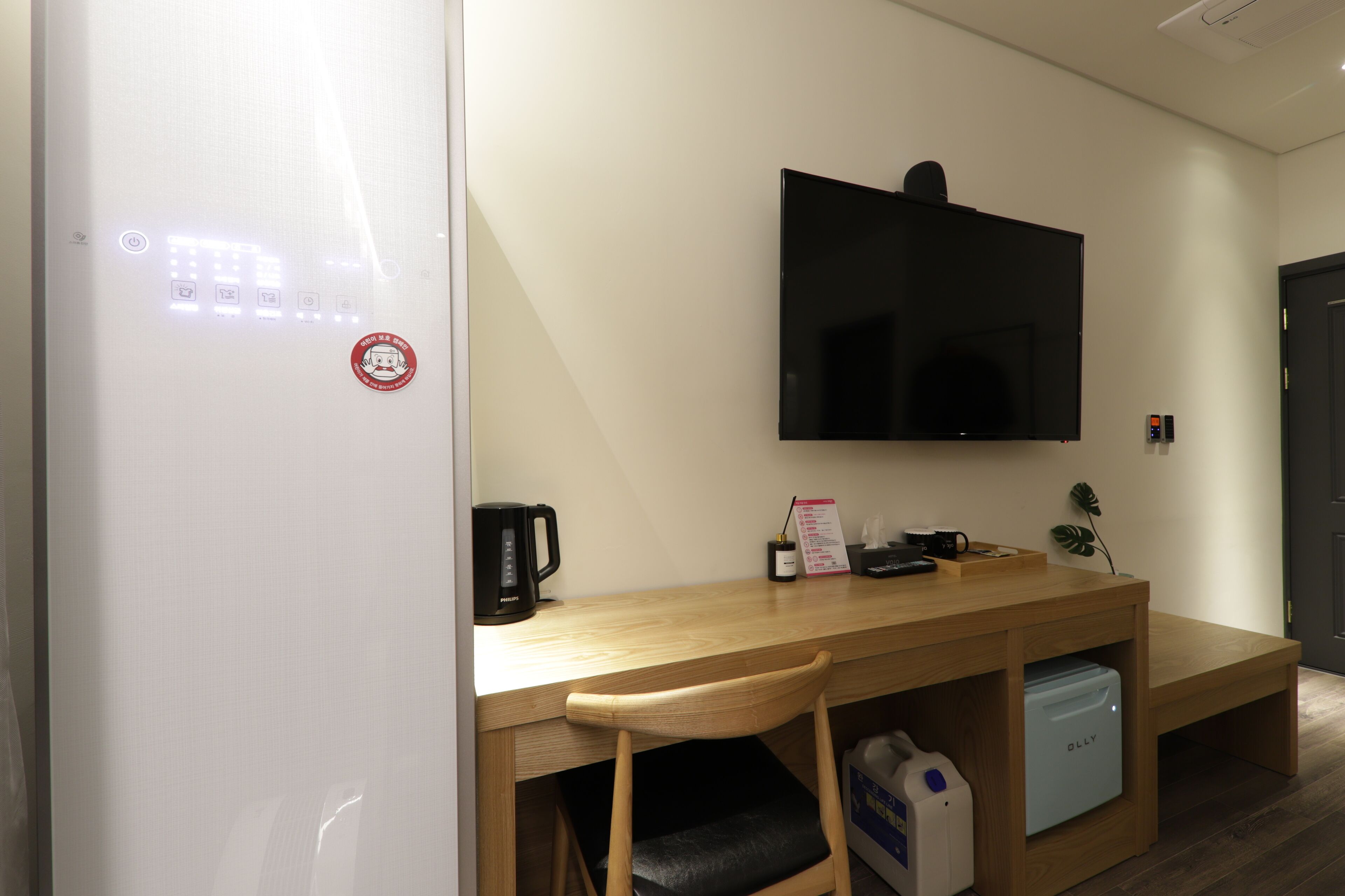 Quarto moderno com escrivaninha de madeira, TV de tela plana na parede, cafeteira e um pequeno frigorífico.