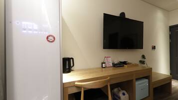 Quarto moderno com escrivaninha de madeira, TV de tela plana na parede, cafeteira e um pequeno frigorífico.
