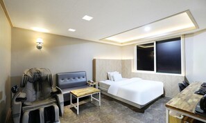 Quarto de hotel com cama, sofá, cadeira de massagem, escrivaninha e janela.