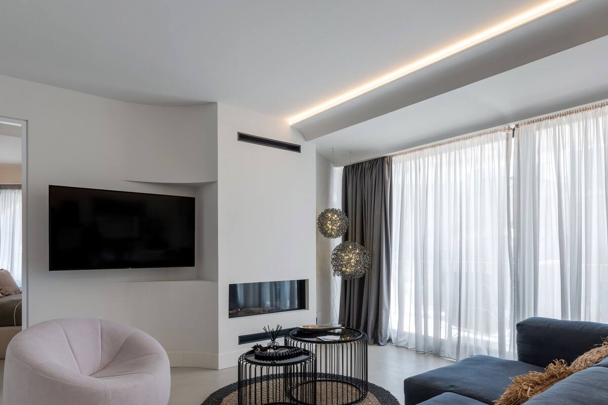 Uma sala de estar moderna com uma televisão de tela plana, lareira e uma janela grande com cortinas leves.