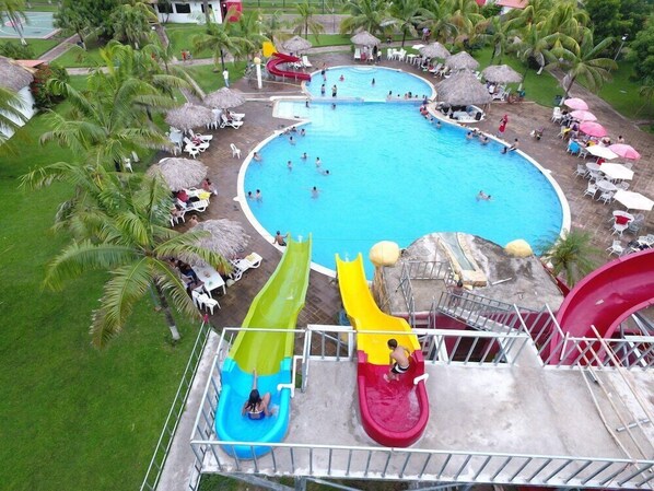 Uma grande piscina ao ar livre com várias escorregas e áreas de descanso.