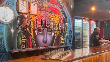 Um bar com um mural colorido, um balcão de madeira e uma estante com torneiras de cerveja.