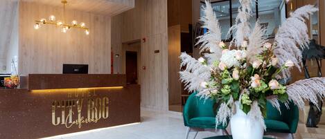 Uma área de recepção de hotel com um balcão de madeira, um sofá verde e um vaso de flores.