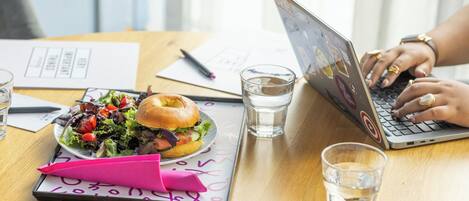 Um laptop sobre uma mesa de madeira com um sanduíche e um copo de água perto.