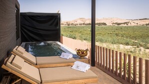 Uma banheira de hidromassagem com duas espreguiçadeiras, uma tigela de frutas e vista para a paisagem do deserto.