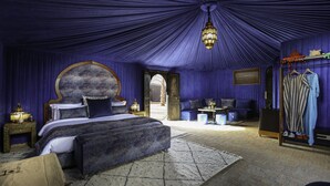 Quarto com cama grande, guarda-roupa e área de estar com mesa e cadeiras.