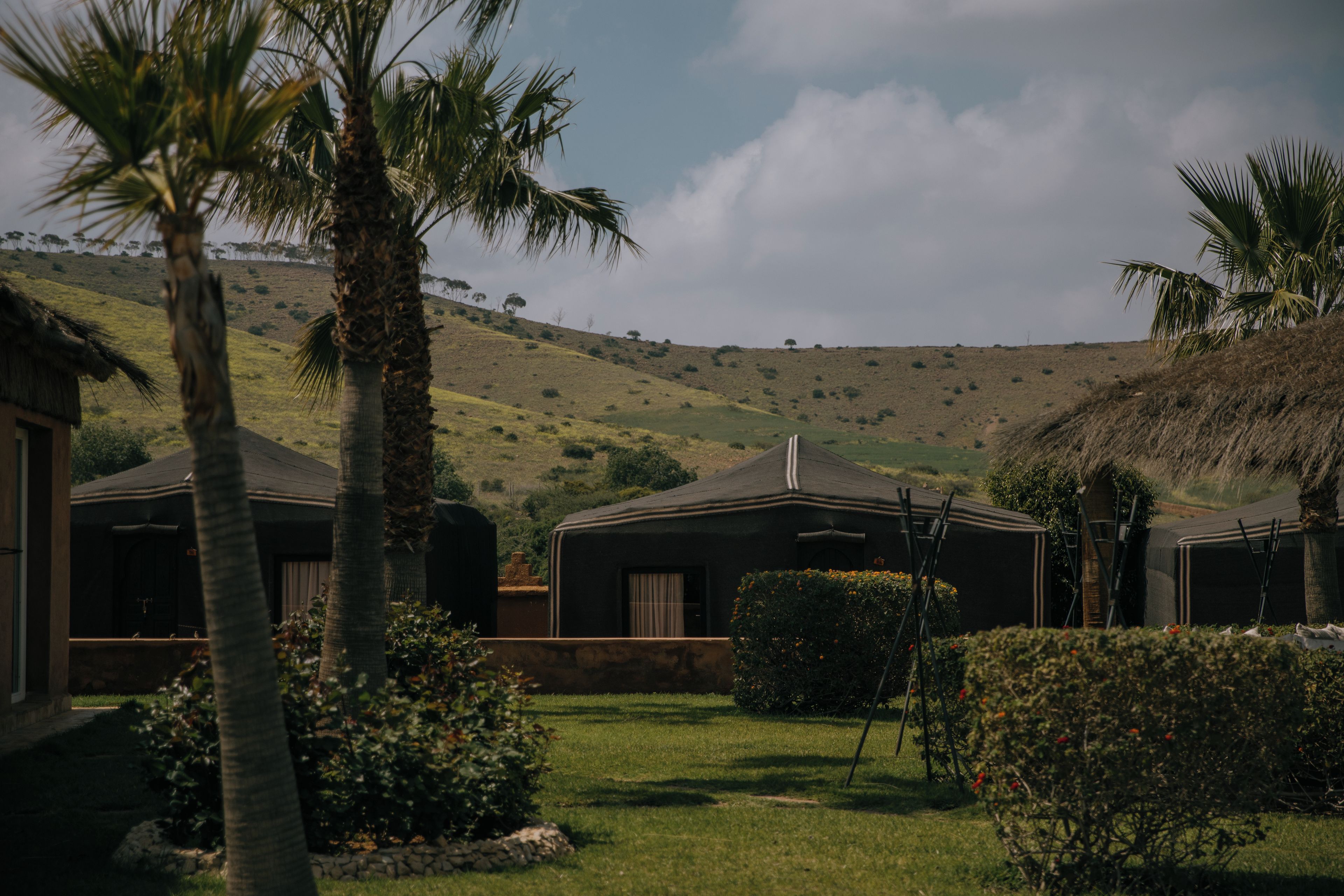 Um resort com cabanas de telhado de palha, palmeiras e uma paisagem montanhosa ao fundo.