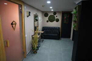 Uma área de recepção com um sofá de couro preto, um espelho e um vaso de planta.