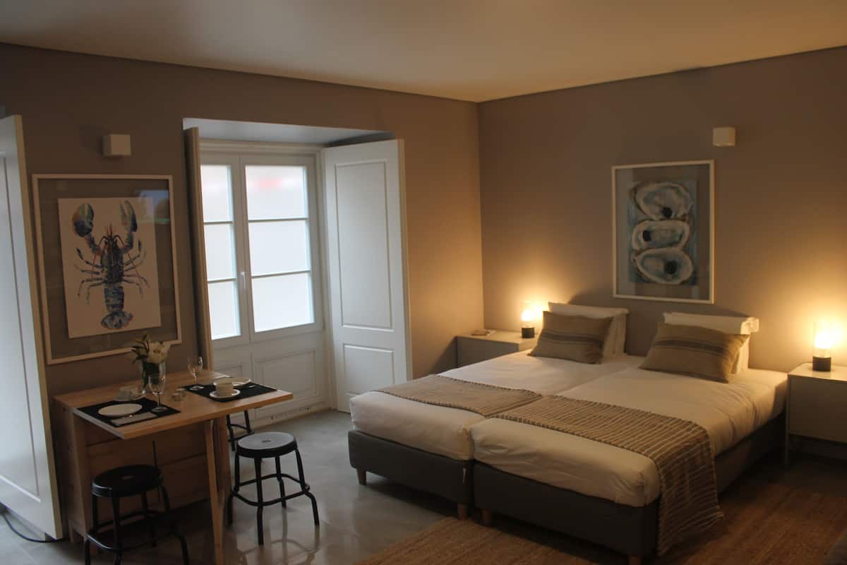 Quarto com cama, mesas de cabeceira, escrivaninha com cadeira e obras de arte nas paredes.
