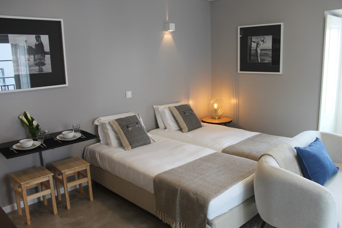 Quarto moderno com duas camas, uma mesa pequena com um vaso de flores e quadros nas paredes.