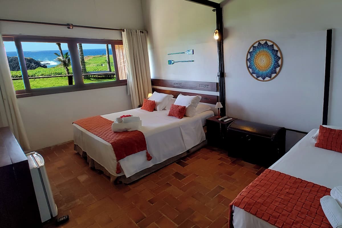 Quarto de hotel com duas camas, vista para o oceano, um ornamento na parede e uma mesa de cabeceira com abajur.