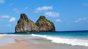 Uma praia com uma formação rochosa imponente ao fundo.