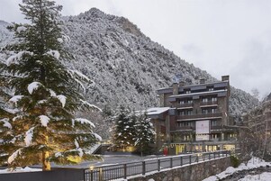 Hotel com vista para montanhas, com um edifício de vários andares, varandas e um letreiro de restaurante.