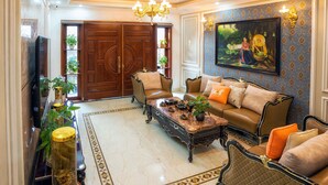 Uma sala de estar espaçosa com uma grande porta de madeira, um conjunto de sofás, uma mesa de centro e um quadro na parede.