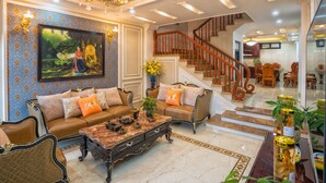 Uma sala de estar ampla com um quadro grande, um candelabro e uma escadaria que leva a uma área de jantar.
