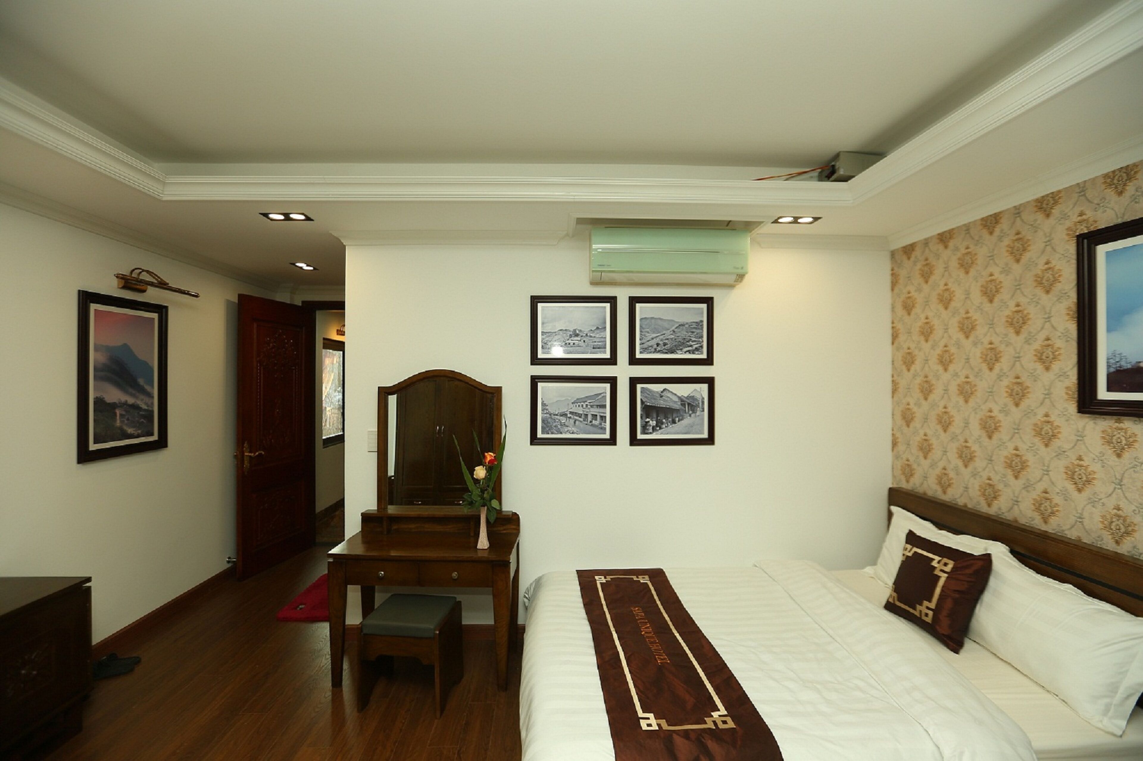 Quarto de hotel com cama, escrivaninha e cadeira. Quatro quadros emoldurados na parede.