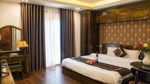 Quarto de hotel com cama grande, mobiliário de madeira, uma secretária e área de refeições.