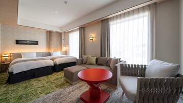 Quarto de hotel com duas camas, um sofá, uma mesa vermelha e uma cadeira.