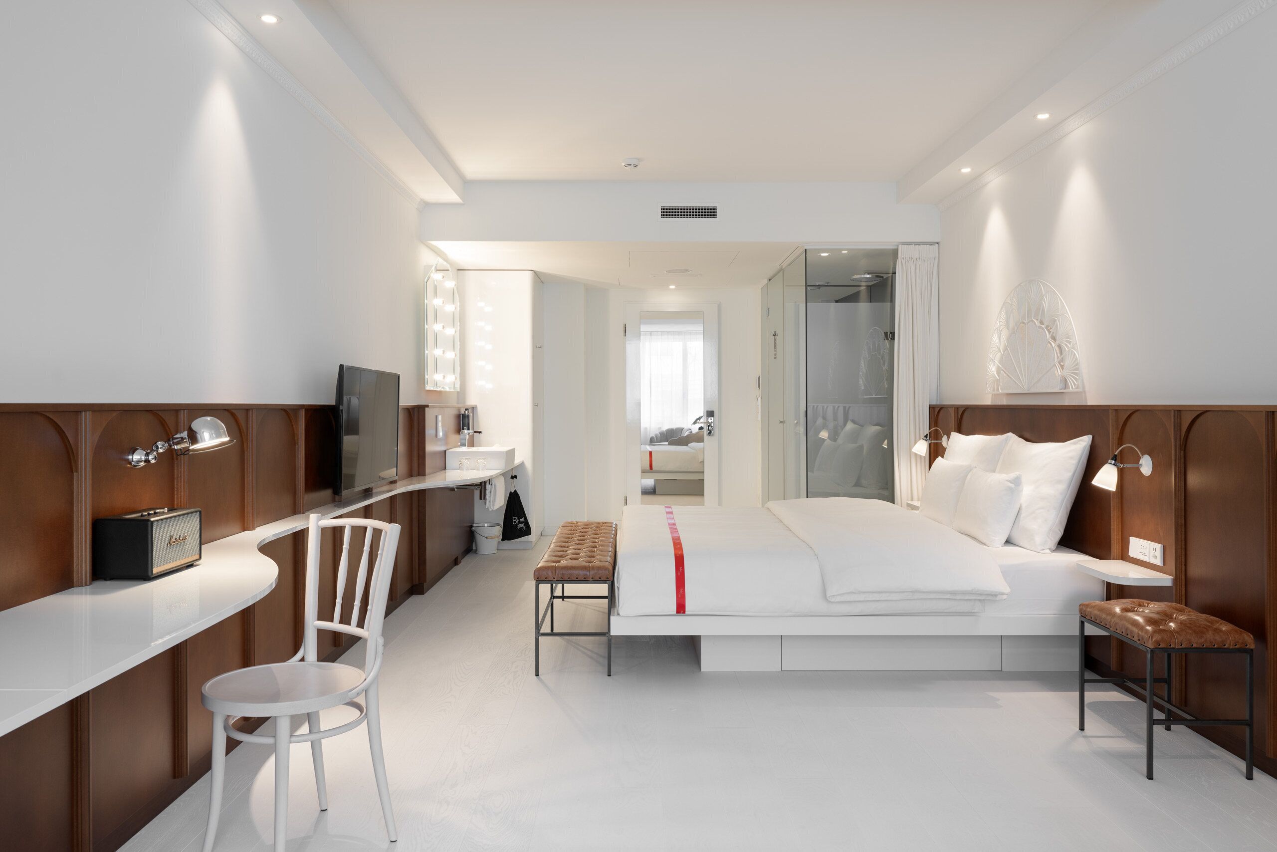 Quarto de hotel moderno com cama, mesas de cabeceira, escrivaninha com cadeira, televisão e banheiro visível por uma porta aberta.