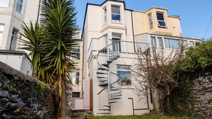 Um edifício residencial com escadaria em espiral, parede de pedra e uma palmeira.