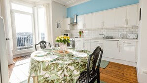 Uma sala de jantar com mesa posta para quatro pessoas, armários brancos, uma parede azul e vista através de uma porta.