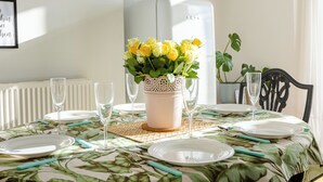 Mesa de jantar posta com pratos, talheres e um vaso de flores amarelas.