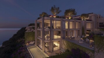 Um edifício moderno de vários andares com fachada de vidro, área de estar externa e vista para o mar.
