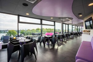 Restaurante moderno com janelas amplas que oferecem vista para a cidade e áreas verdes.