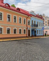 Rua de paralelepípedos com edifícios de arquitetura clássica, incluindo um edifício azul com varanda e um edifício vermelho com telhado vermelho.
