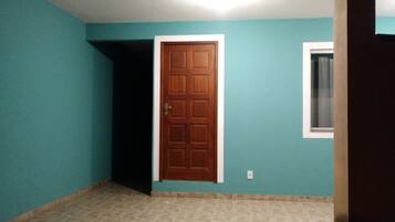 Quarto com paredes verde-água, porta de madeira, janela com cortina e piso ladrilhado.