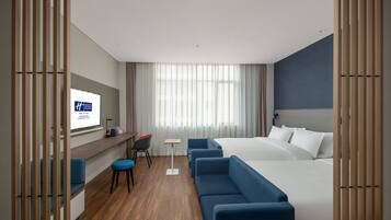 Quarto de hotel com uma cama grande, uma escrivaninha com computador, uma cadeira e televisão na parede.