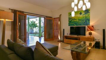 Uma sala de estar moderna com sofá, TV, mesa de centro de vidro e um quadro de paisagem tropical.