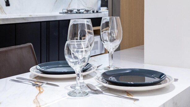 Uma cozinha moderna com bancada de mármore, duas taças de vinho e pratos postos para refeição.